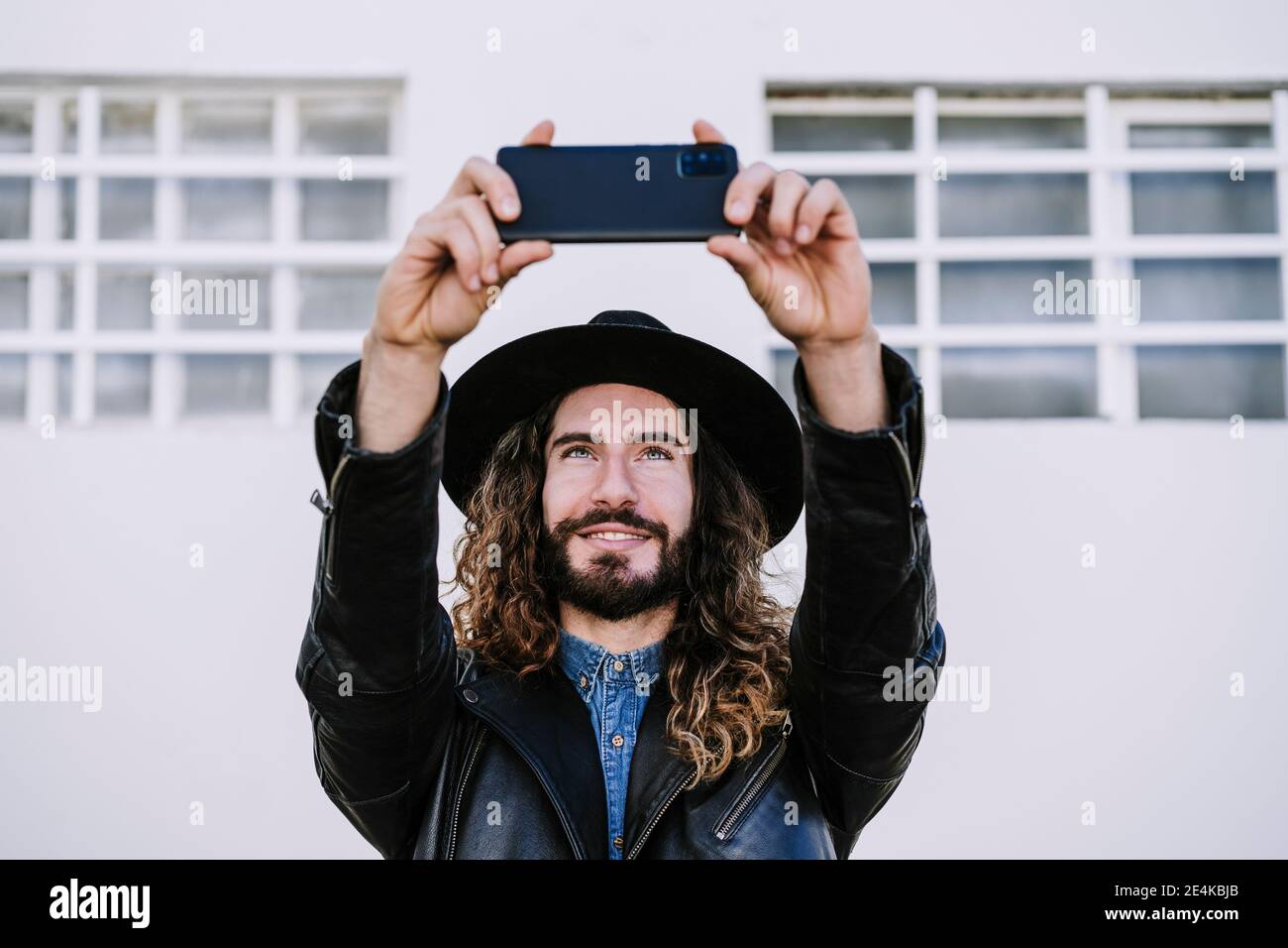 Fashionable young man taking selfie through smart phone against white ...