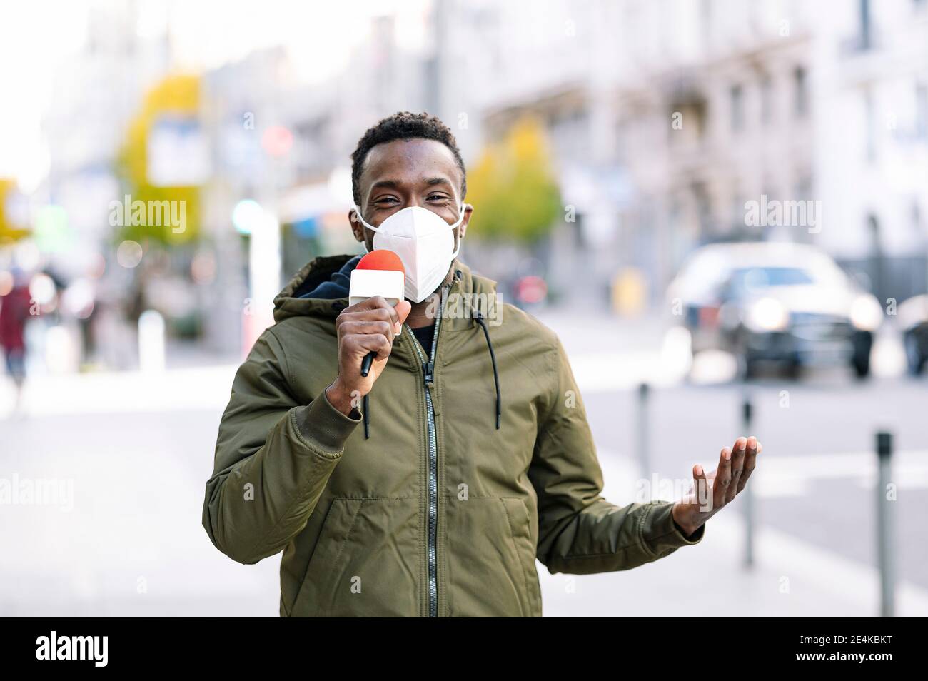 Male presenter wearing face mask talking over microphone while standing ...