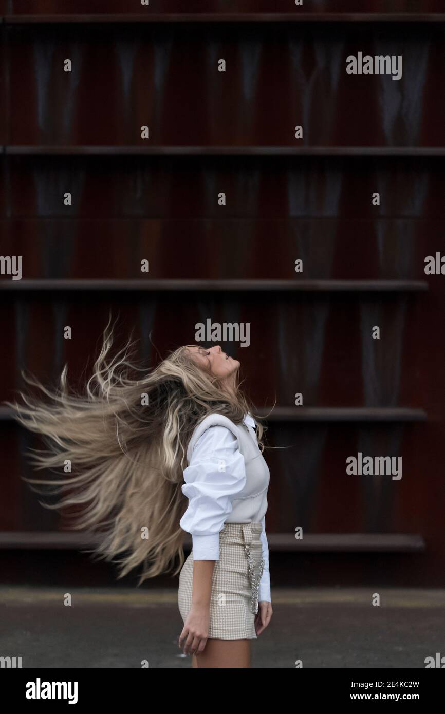 Fashionable woman with eyes closed tossing hair in front of wall Stock ...