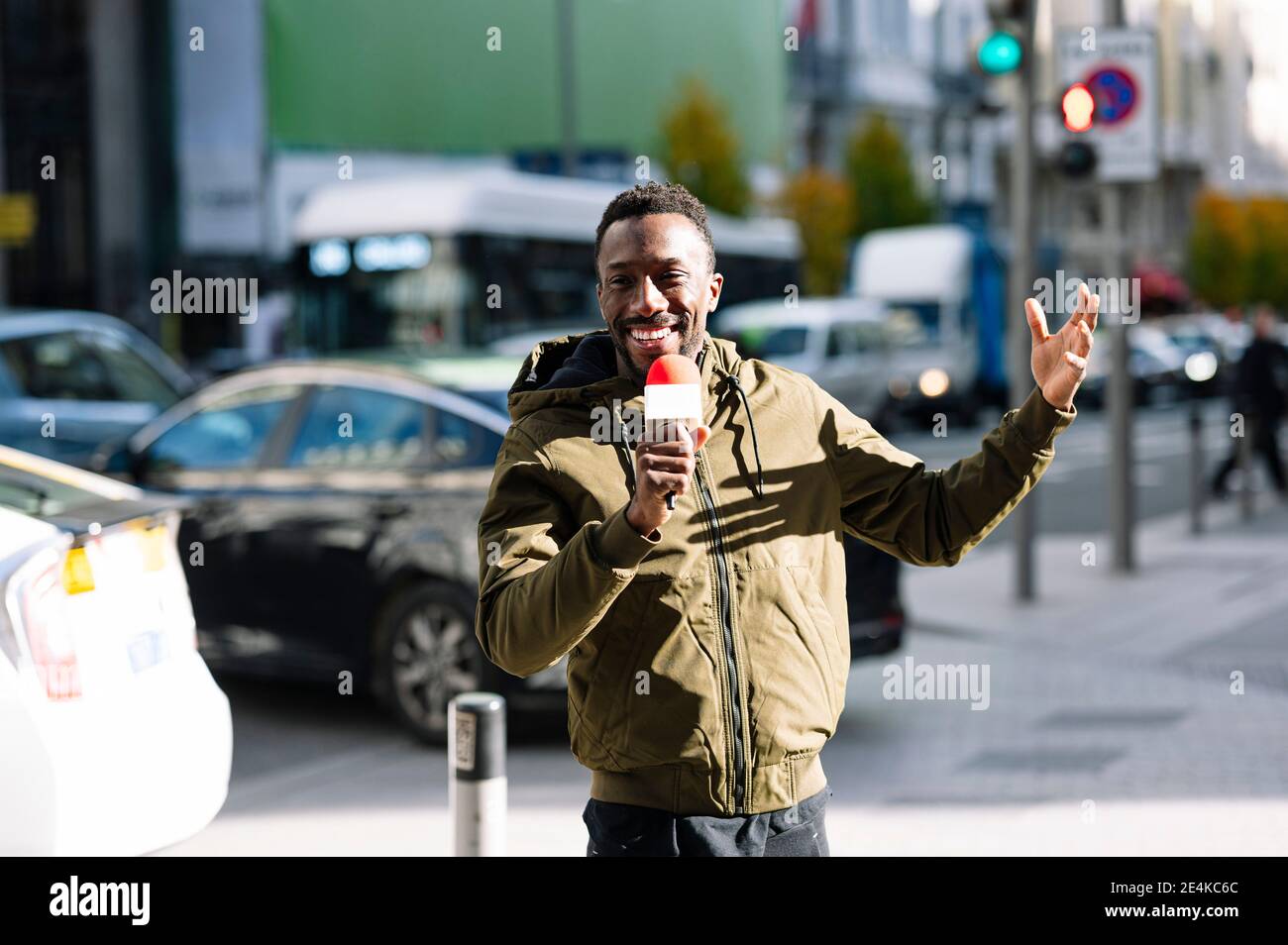 Smiling male reporter talking over microphone while standing on street ...