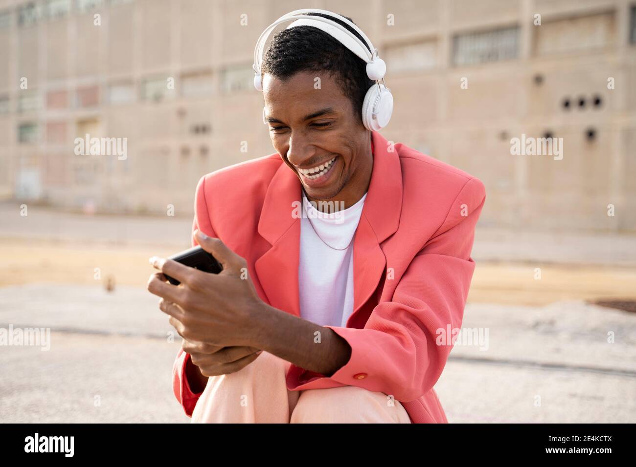 Happy man wearing headphones using mobile phone while sitting outdoors ...