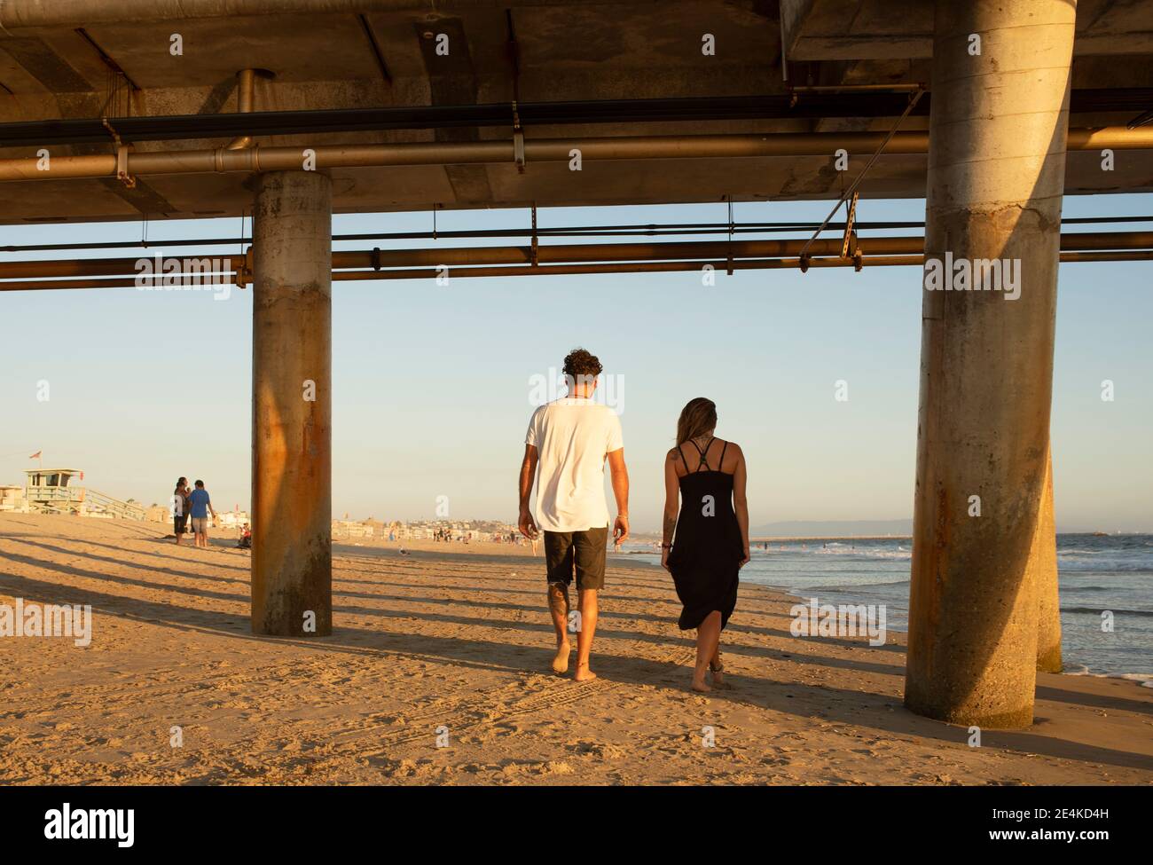Rear view of young people walking below Venice Pier. Sunset vibes at ...