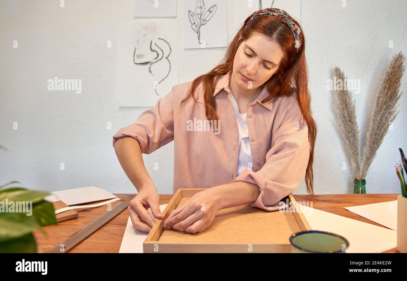 Female artist closing picture frame at desk while working at home Stock ...