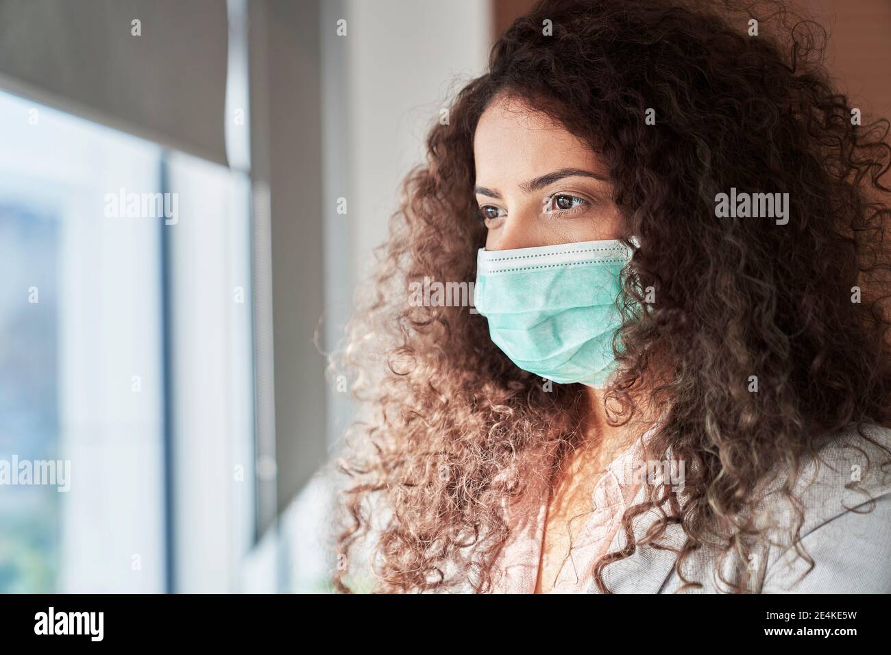 Female professional wearing protective face mask looking through window ...