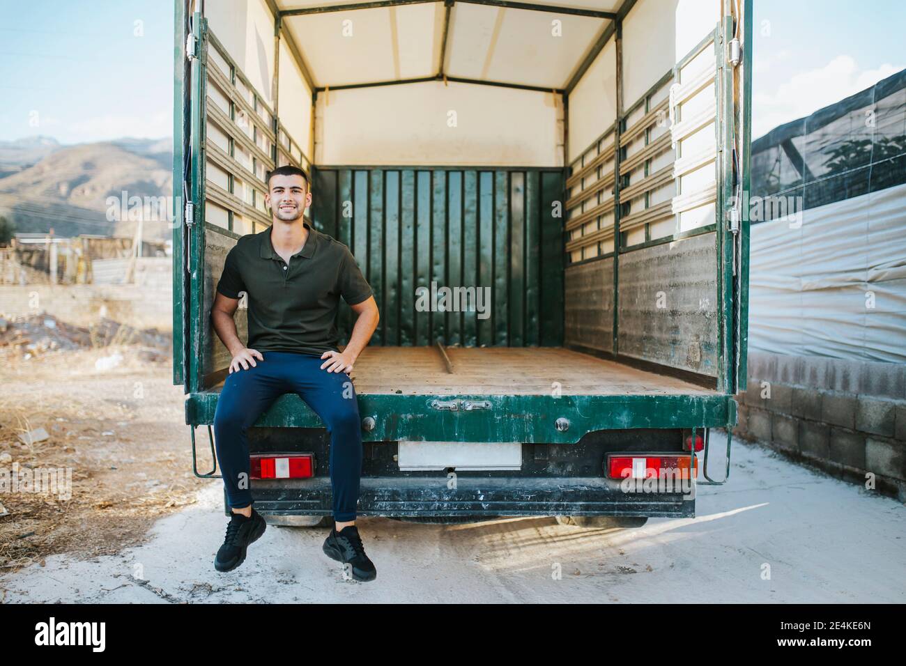 Smiling young male farmer sitting on empty semi-truck outside of ... Smiling young male farmer sitting on empty semi-truck outside of ...