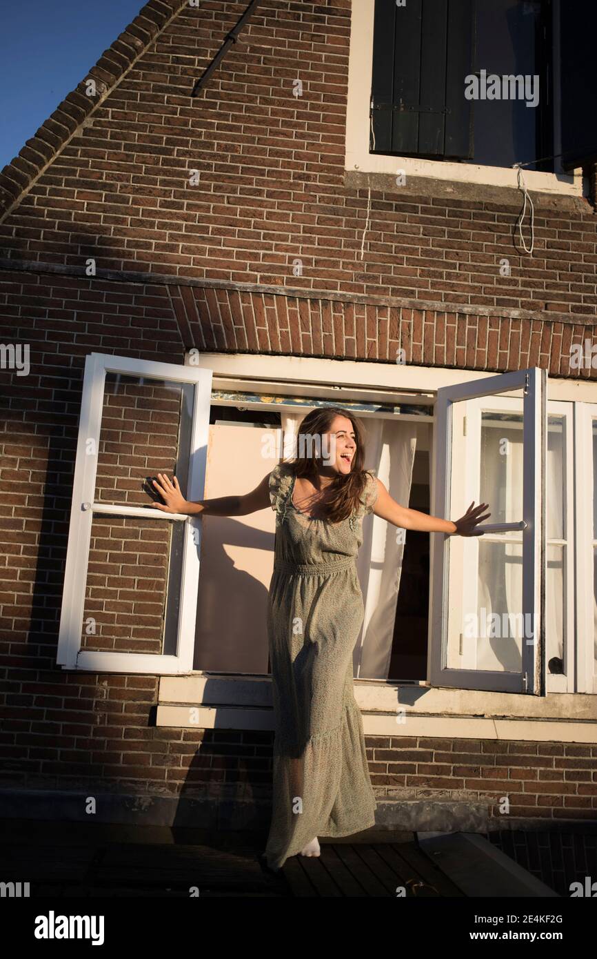 Cheerful woman with arms outstretched screaming while standing by ...