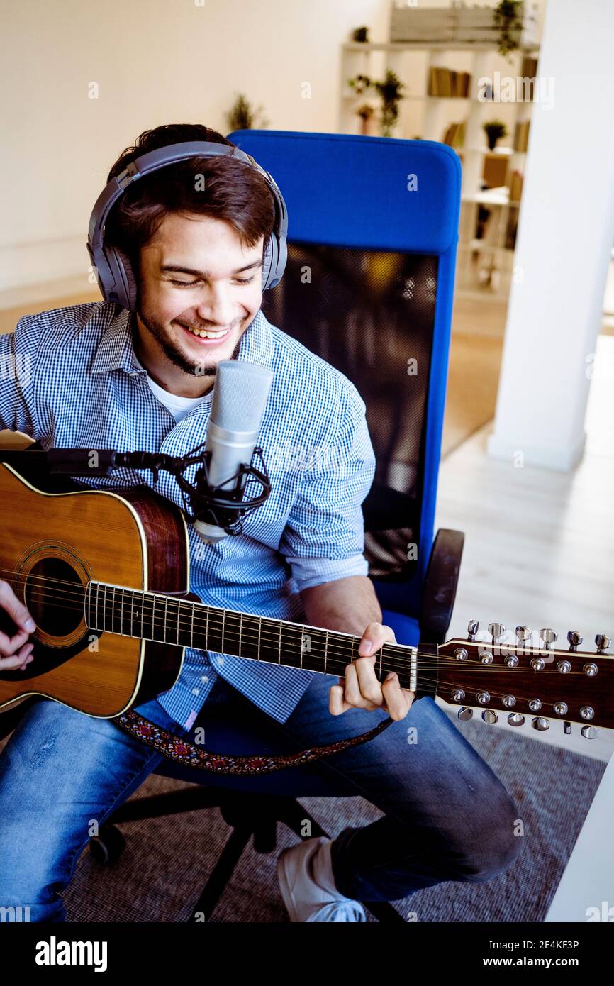 Smiling musician recording music while playing guitar at recording ...