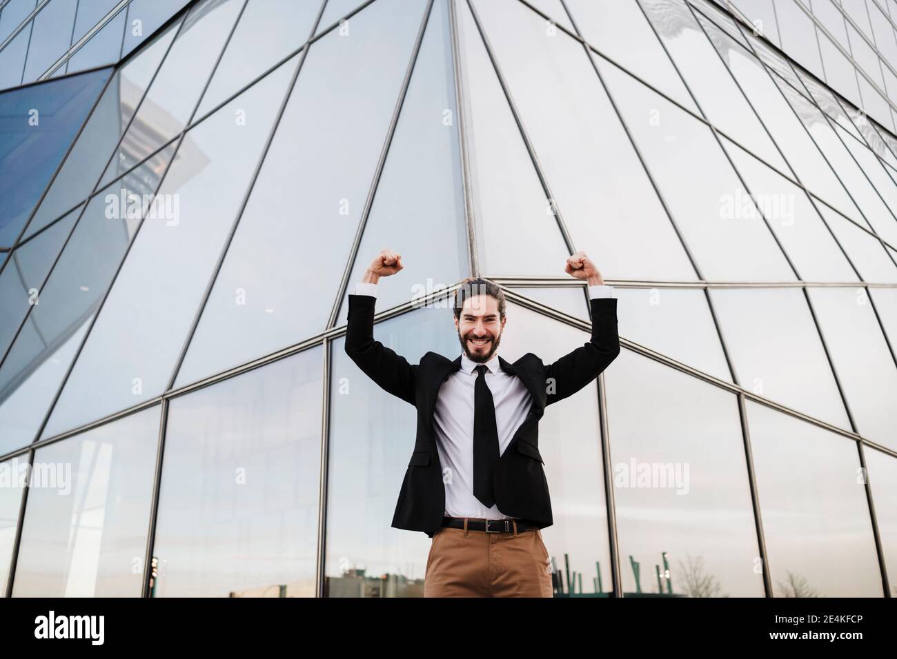 Smiling businessman flexing muscles while standing against building ...