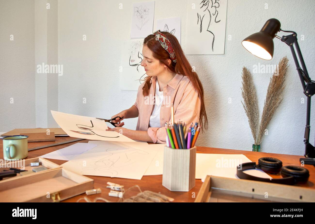 Female freelancer cutting paper edges at desk while working at home ...