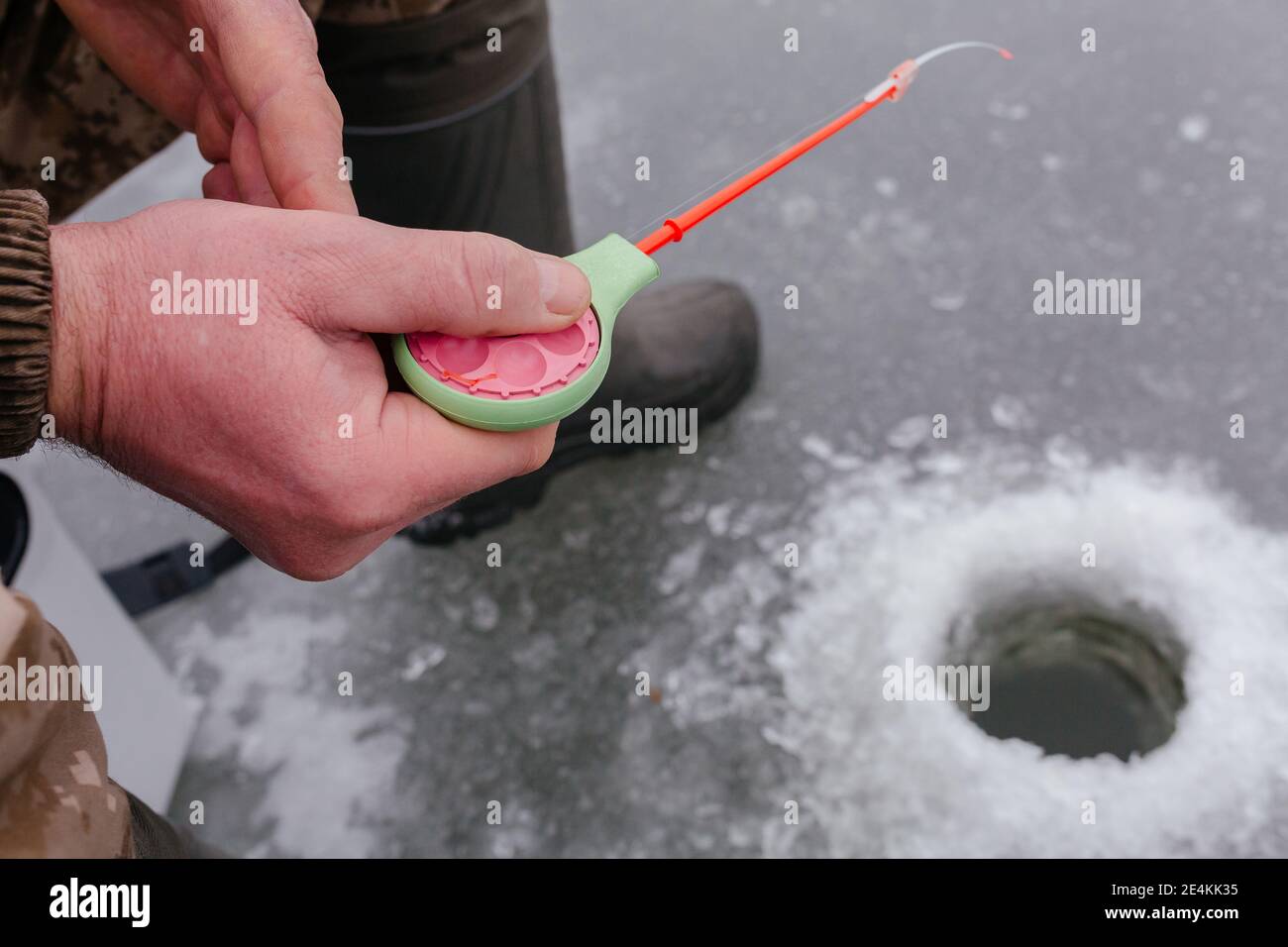 Fisherman with a fishing rod sitting on a frozen river in the winter ...
