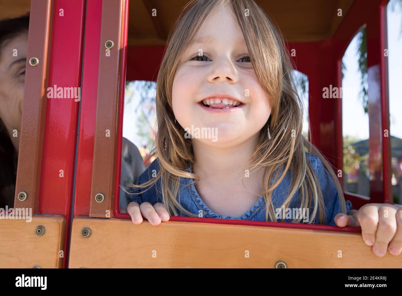 face of four years old blonde girl leaning out the window of playground ...