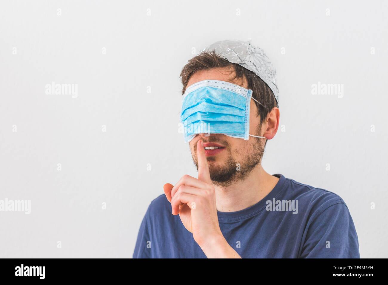 Young angry man with face mask over the eyes and aluminum hat is doing ...