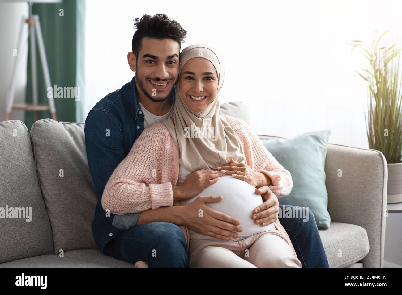 Happy religious muslim couple expecting baby posing on couch at home ...