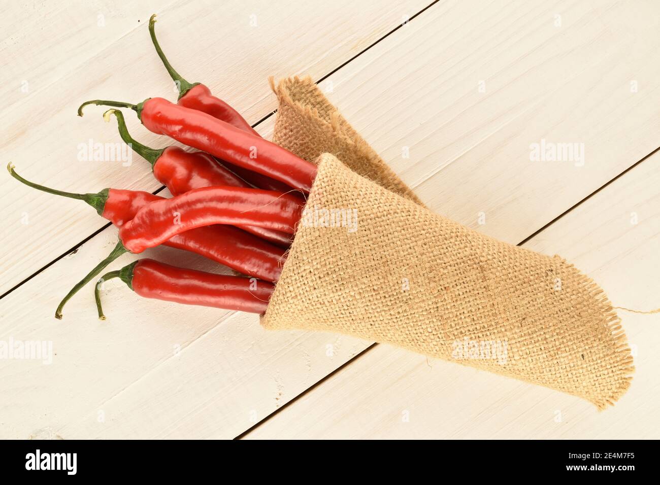 A few pods of ripe bright red fresh hot pepper in a jute bag on a white ...