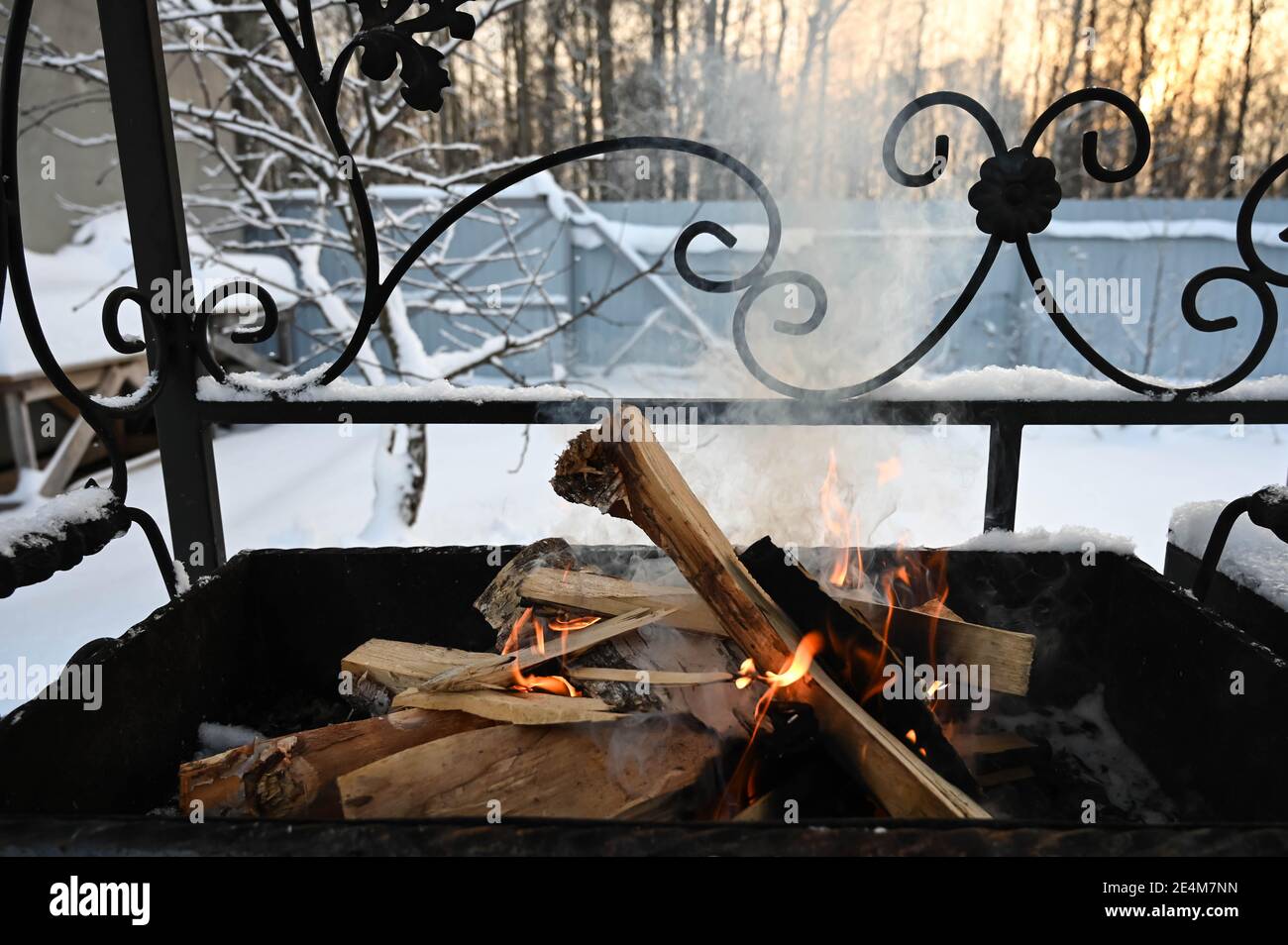 Close-up of burning and smoking wood in wrought iron brazier at winter ...