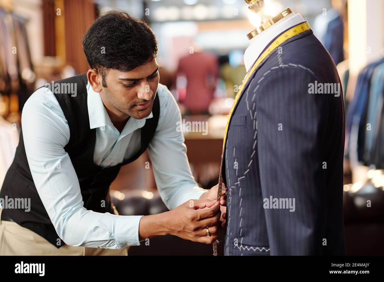 Talented young Indian tailor working on bespoke suit on mannequin, and ...
