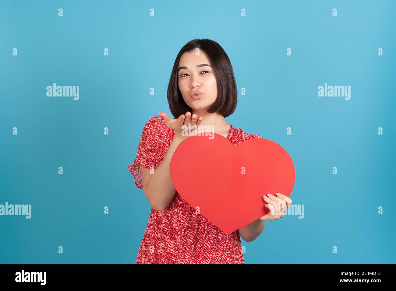 A romantic, lovesick young Asian woman in a red dress holds a large red ...