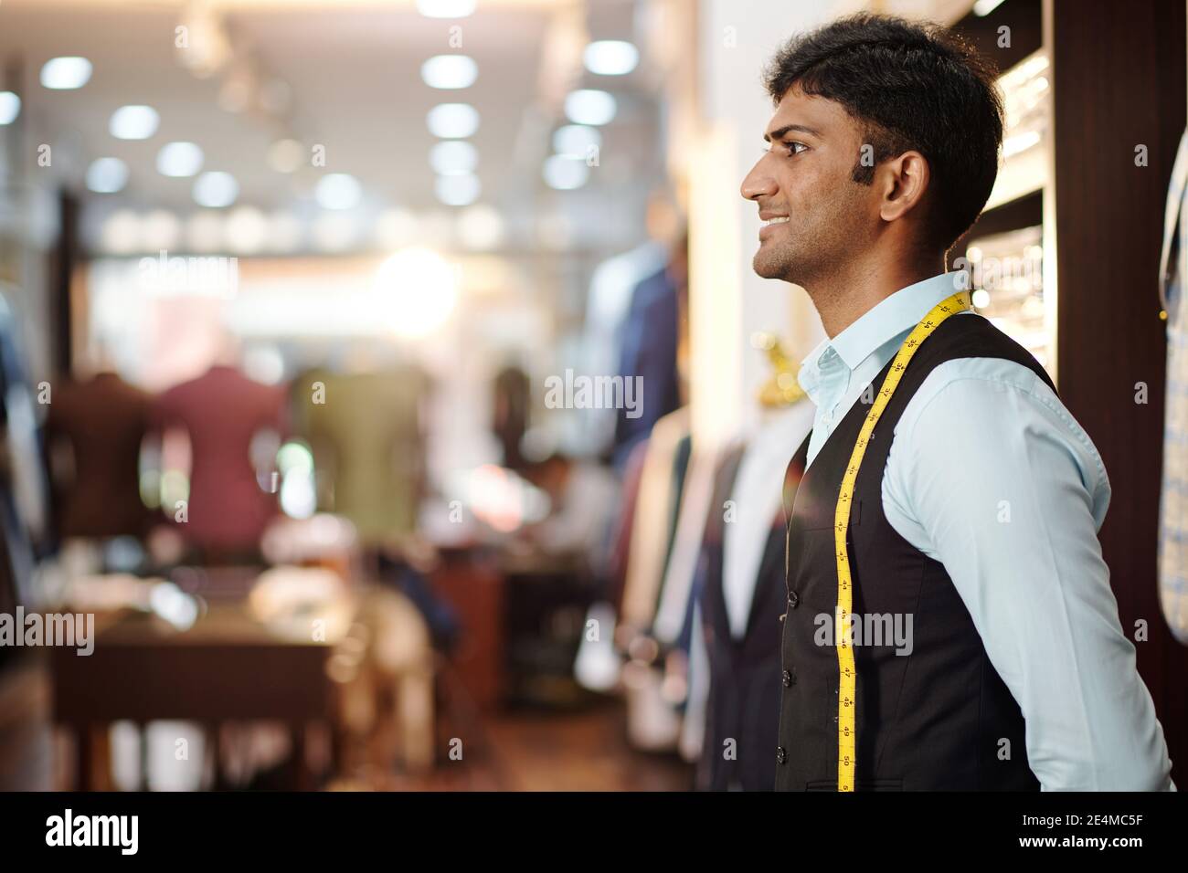 Portrait of happy young Indian tailor with mesuring tape looking at ...
