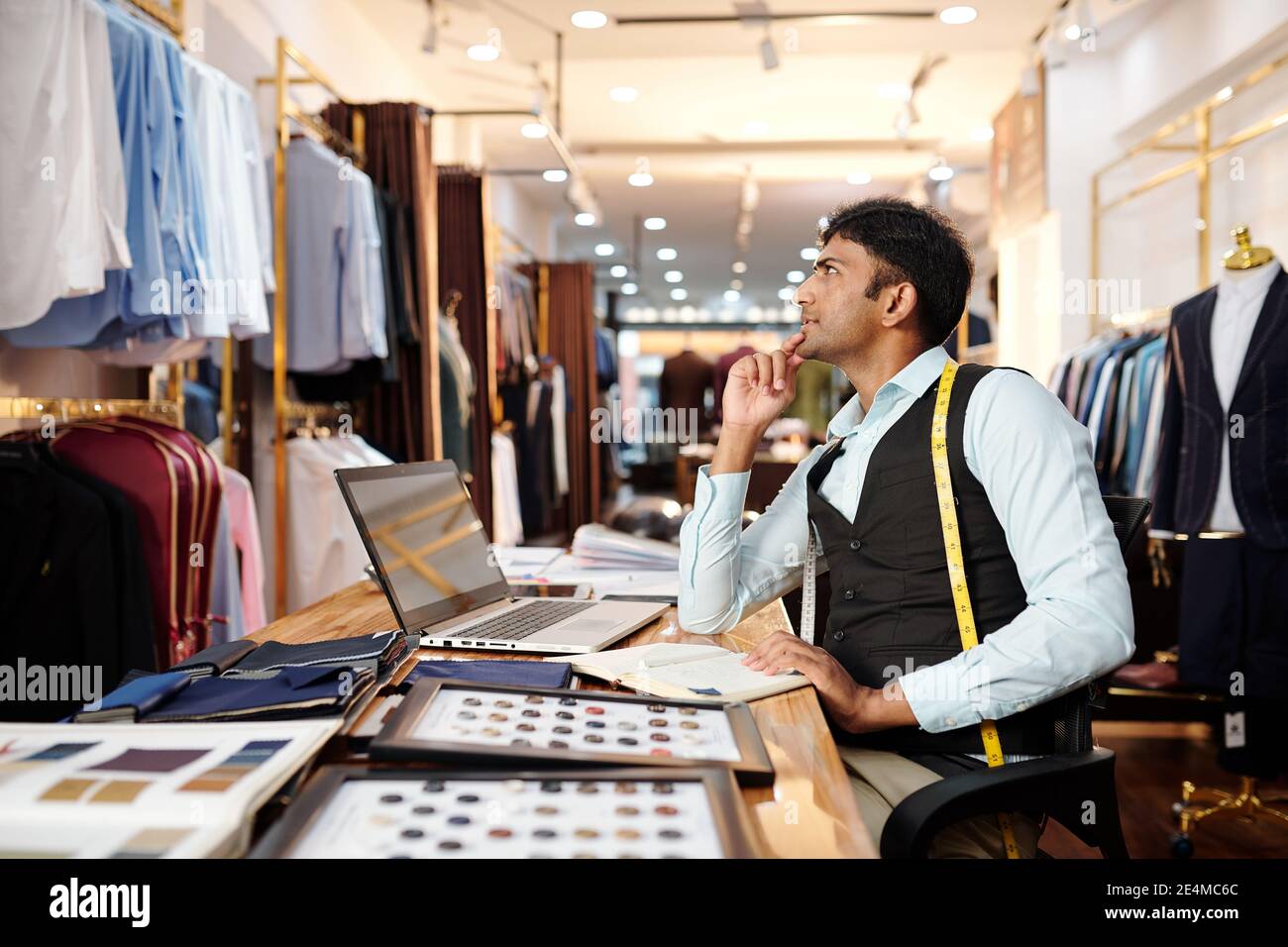 Ttalented young Indian tailor sitting at big table in mens atelier and ...