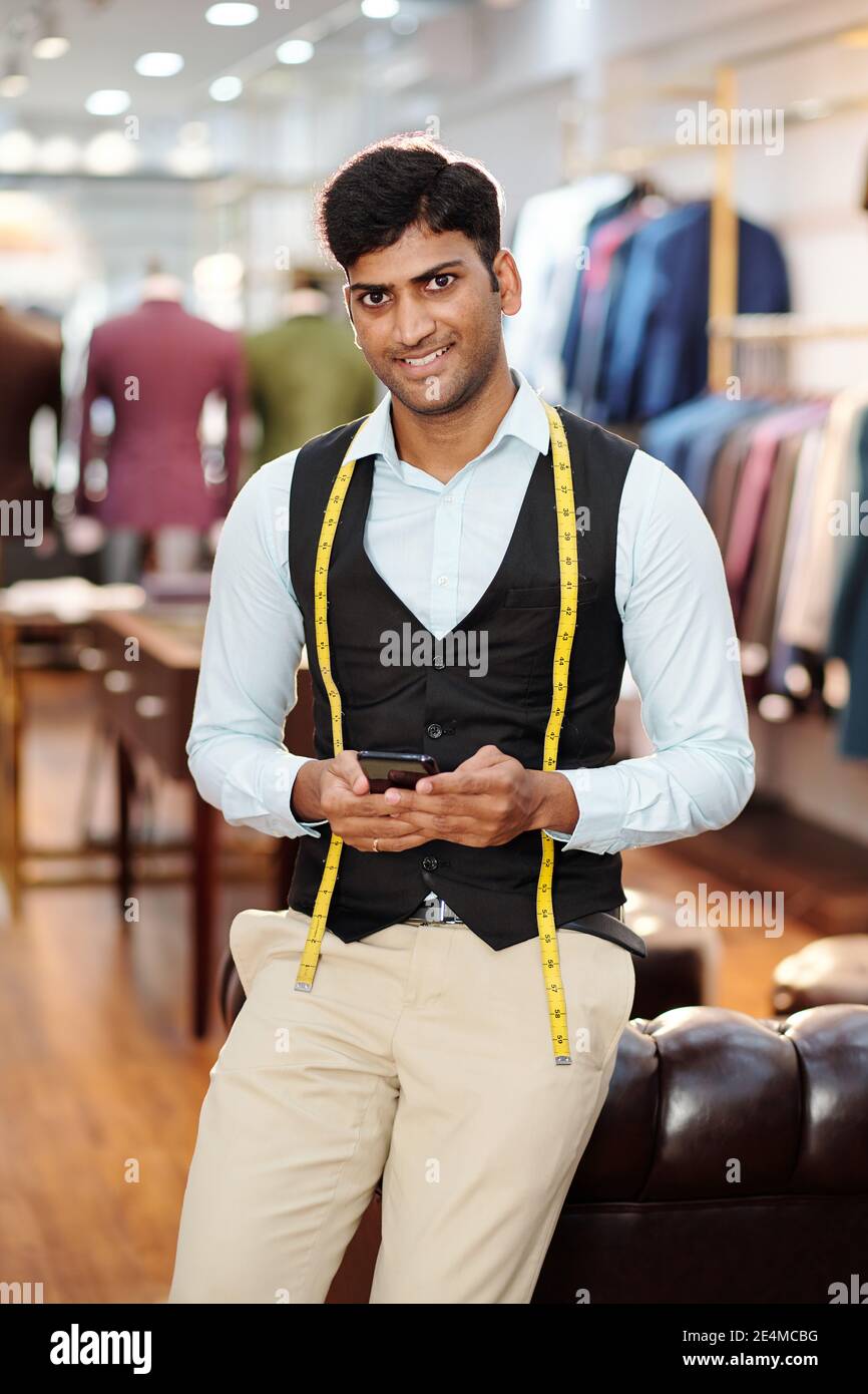 Portrait of smiling handsome young Indian tailor using application on ...