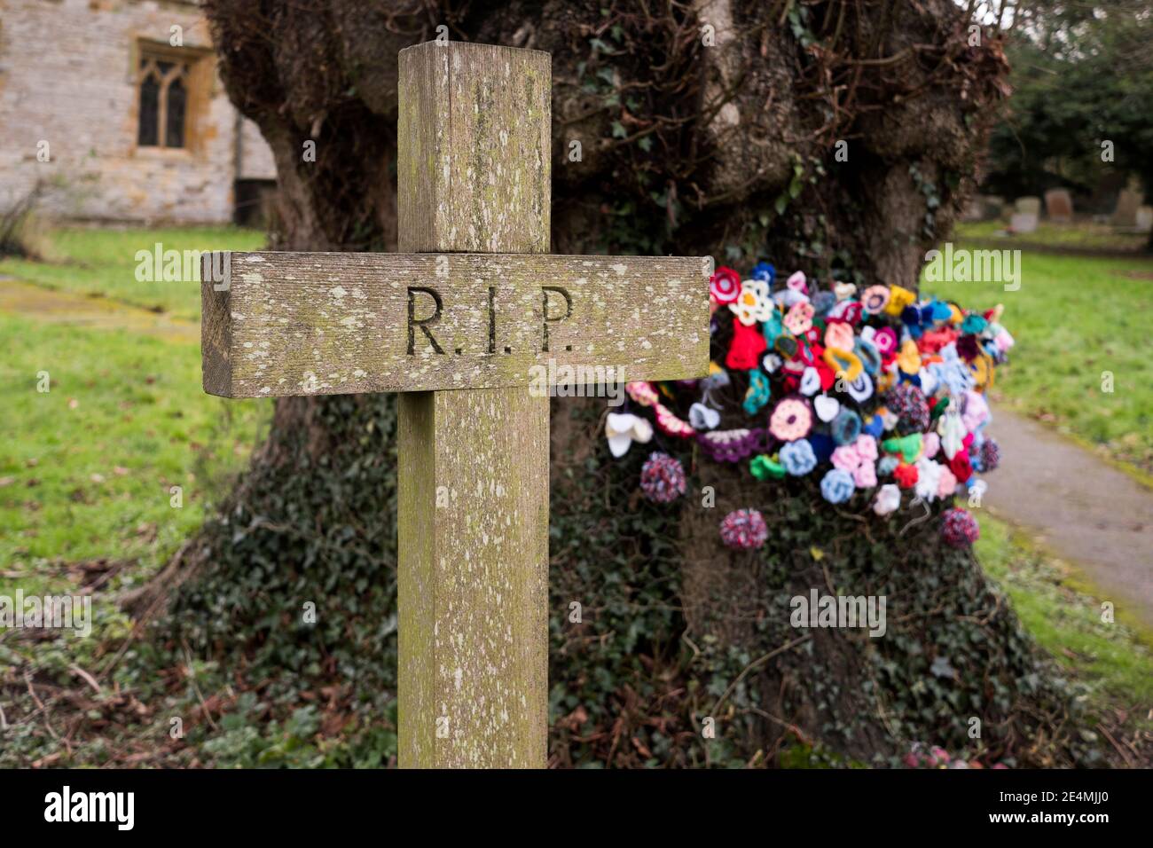 A wooden cross with RIP written on it, with knitted wool flowers on a ...
