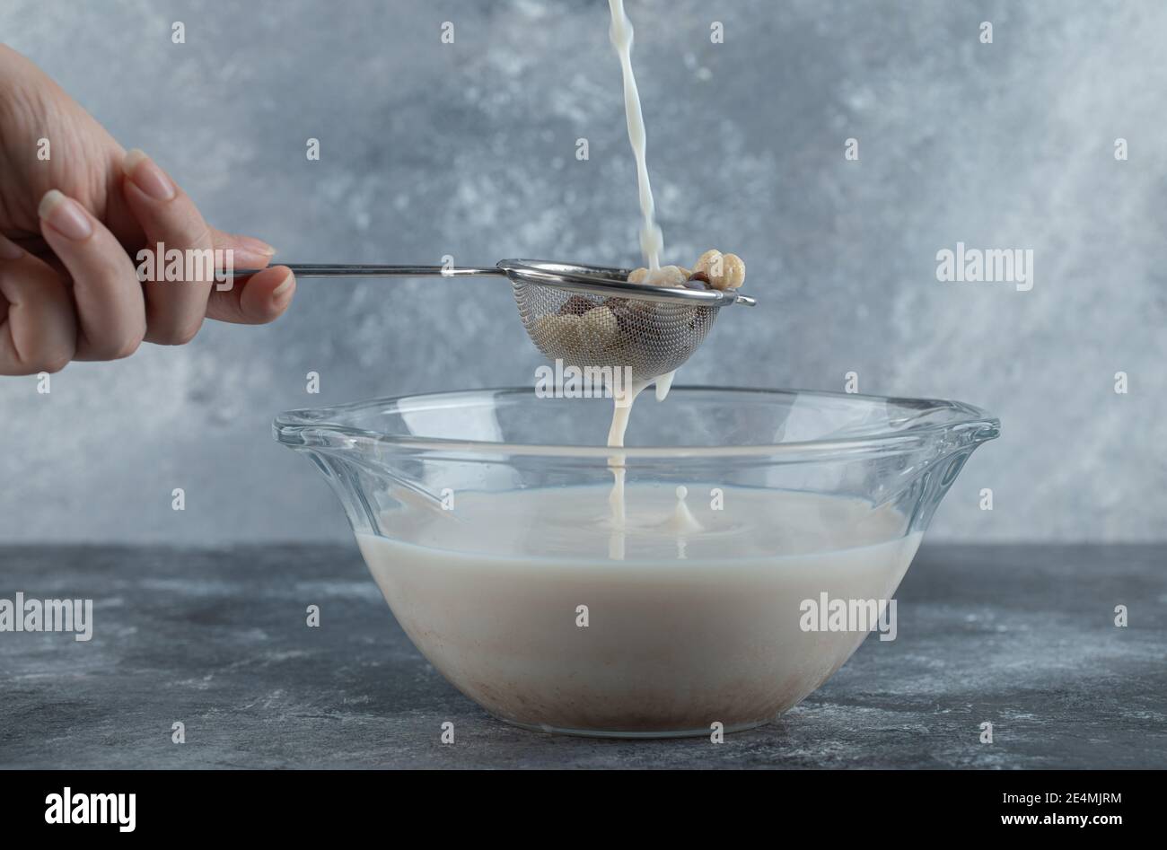 Female hand adding milk into strainer spoon full of cereal balls Stock ...