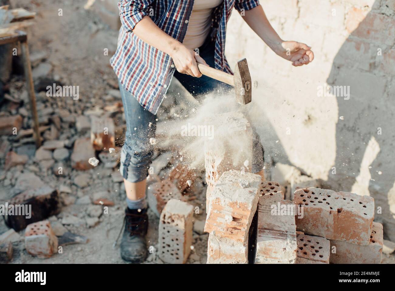 Female constructer breaking a perforated brick with an old hammer Stock ...