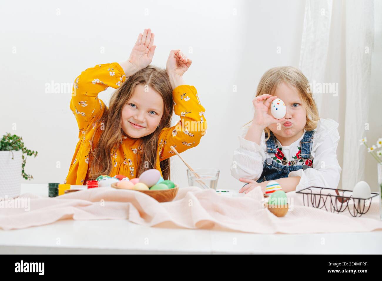 Two little girls sitting behind a table with easter eggs Stock Photo ...