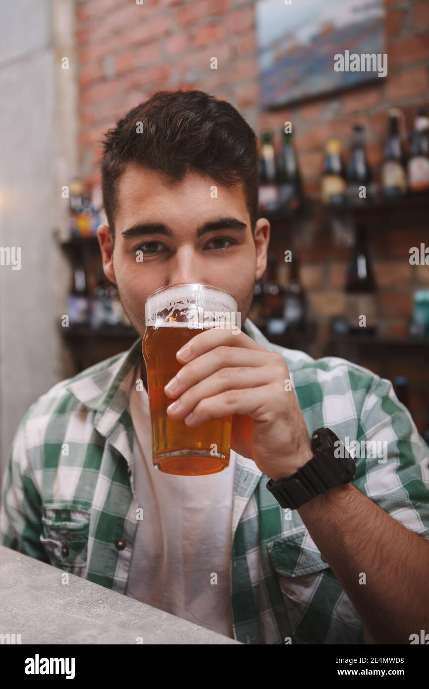 Vertical shot of a handsome man drinking light beer at the beer pub ...