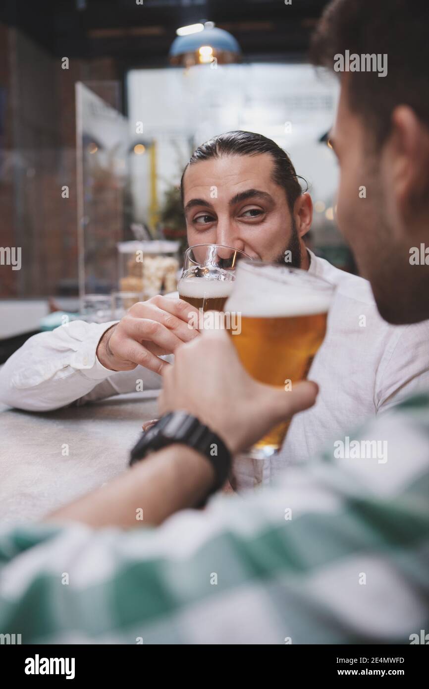 Vertical cropped shot of male friends sipping beer, talking at beer pub ...