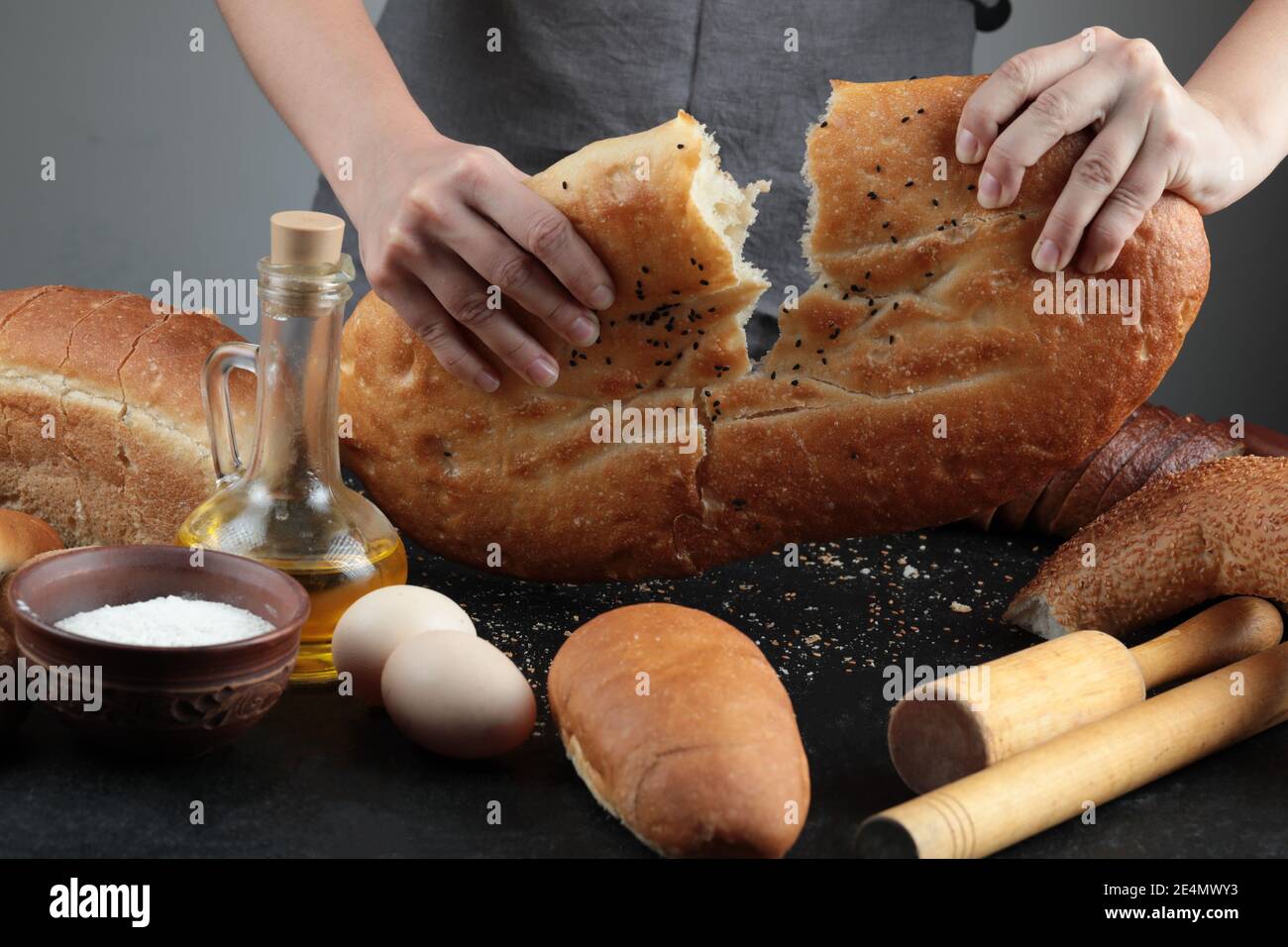 Woman cut bread into half on dark table with eggs, flour bowl and glass ...