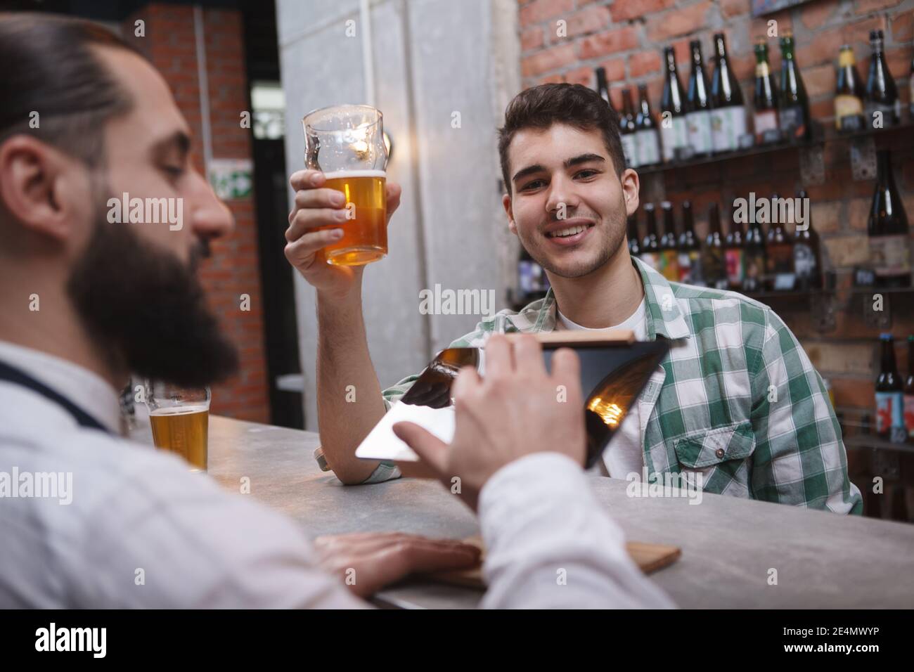 Cheerful handsome man toasting with his beer glass, drinking at the pub ...