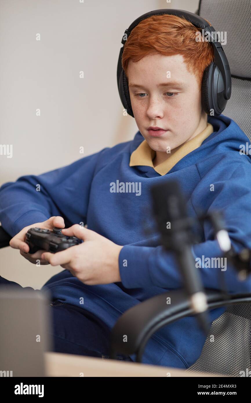 Vertical portrait of red haired teenage boy playing video games and ...