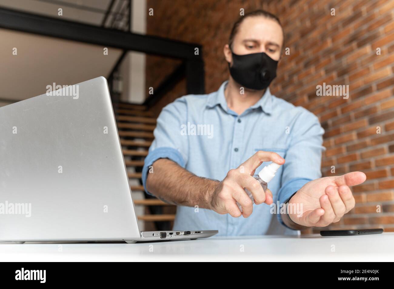 An male office employee wearing mask is spraying antibacterial ...