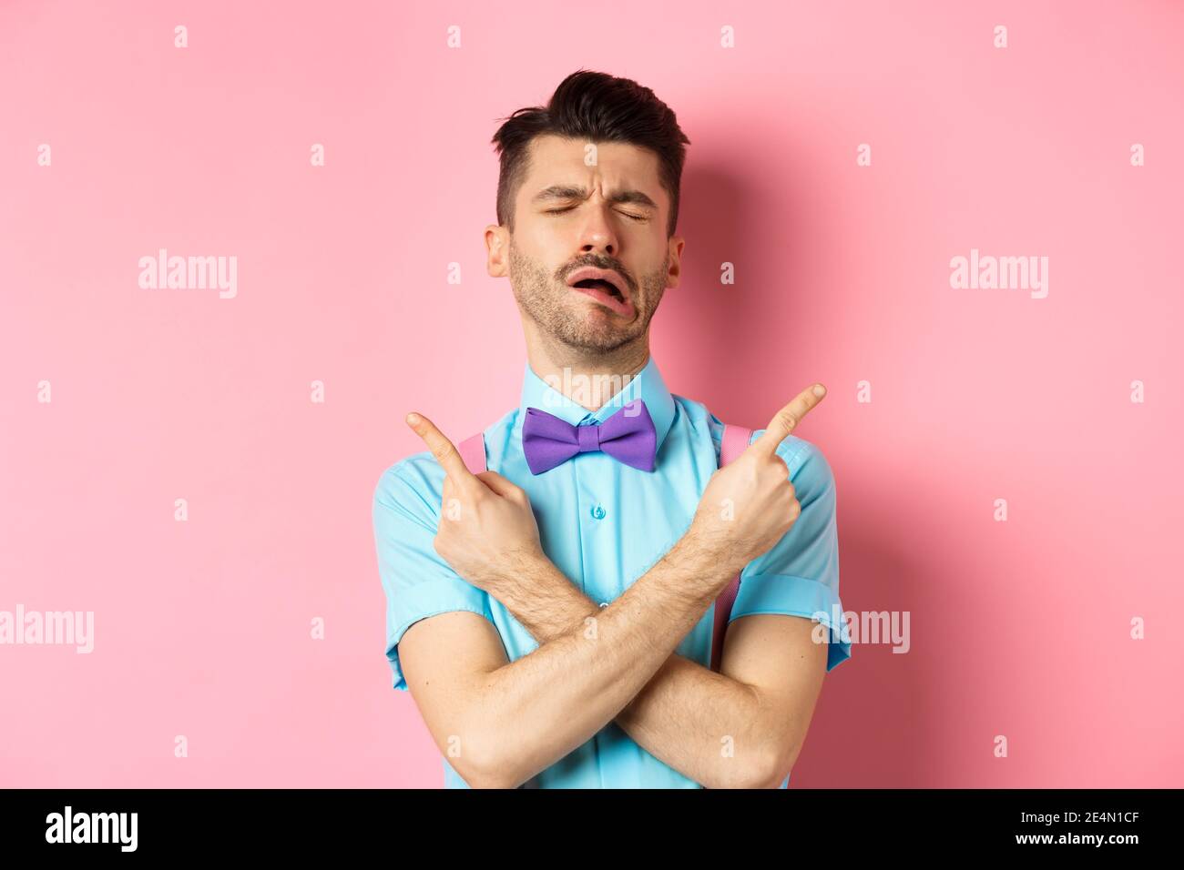 Sad and disappointed young man in bow-tie, crying and pointing fingers ...