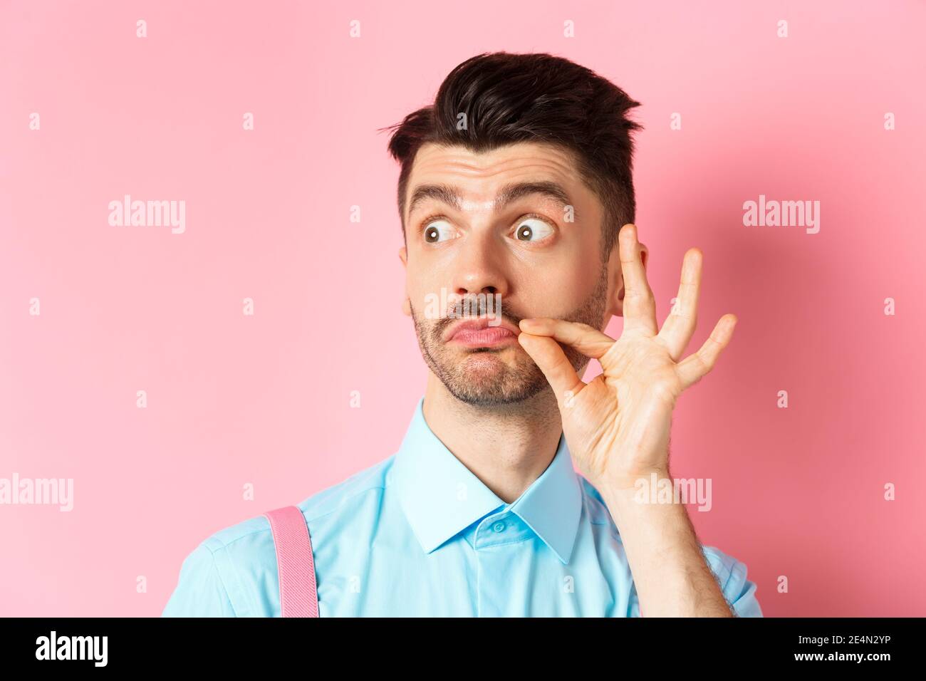 Close up of young caucasian man touching moustache and pucker lips ...