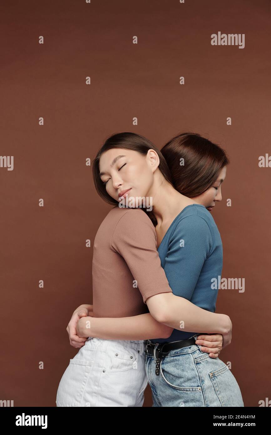 Two young beautiful female twins in casualwear standing in embrace with ...