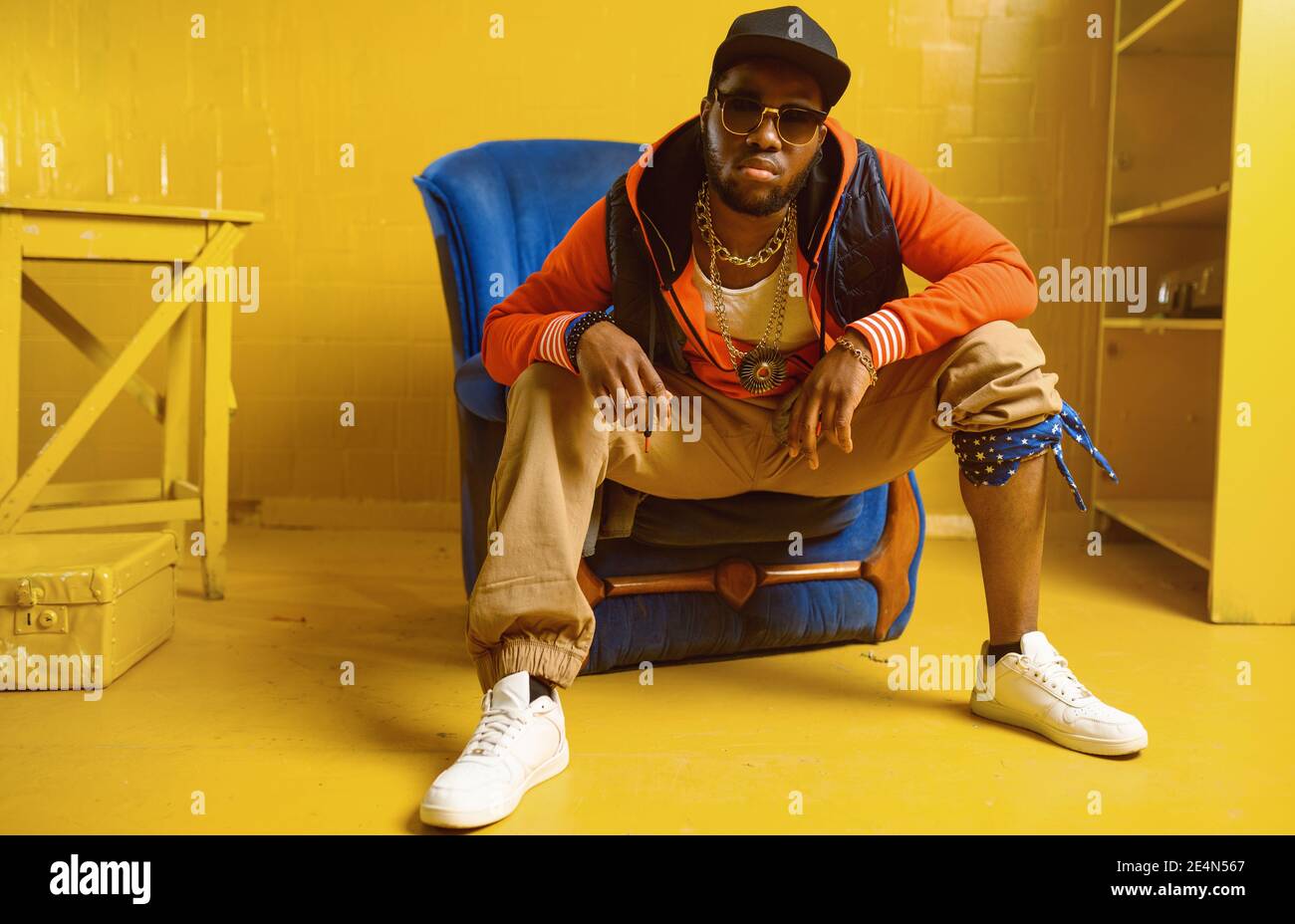 Rapper posing in chair in studio with yellow tones Stock Photo - Alamy