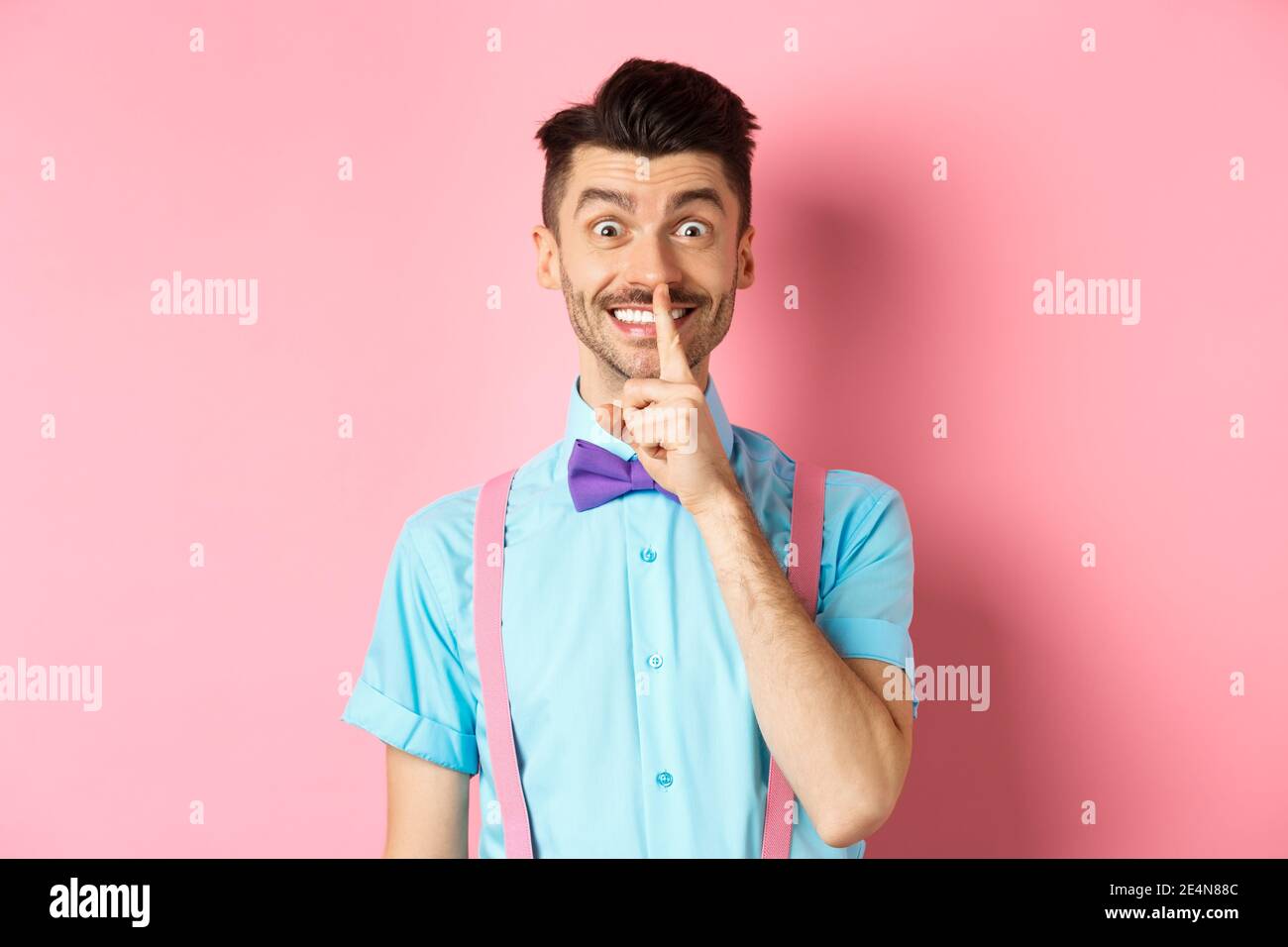 Cheerful young man making surprise, shushing at camera with happy smile ...