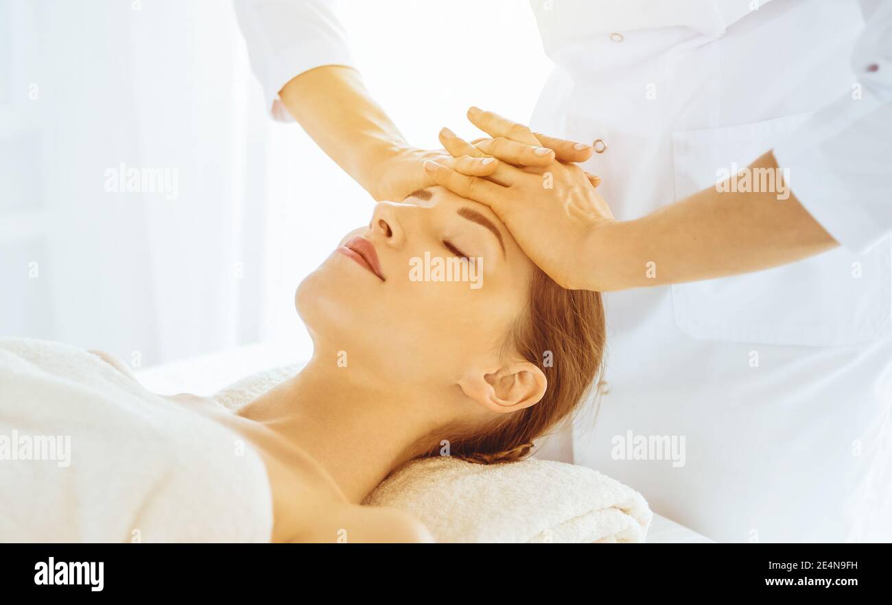 Beautiful woman enjoying facial massage with closed eyes in sunny spa ...