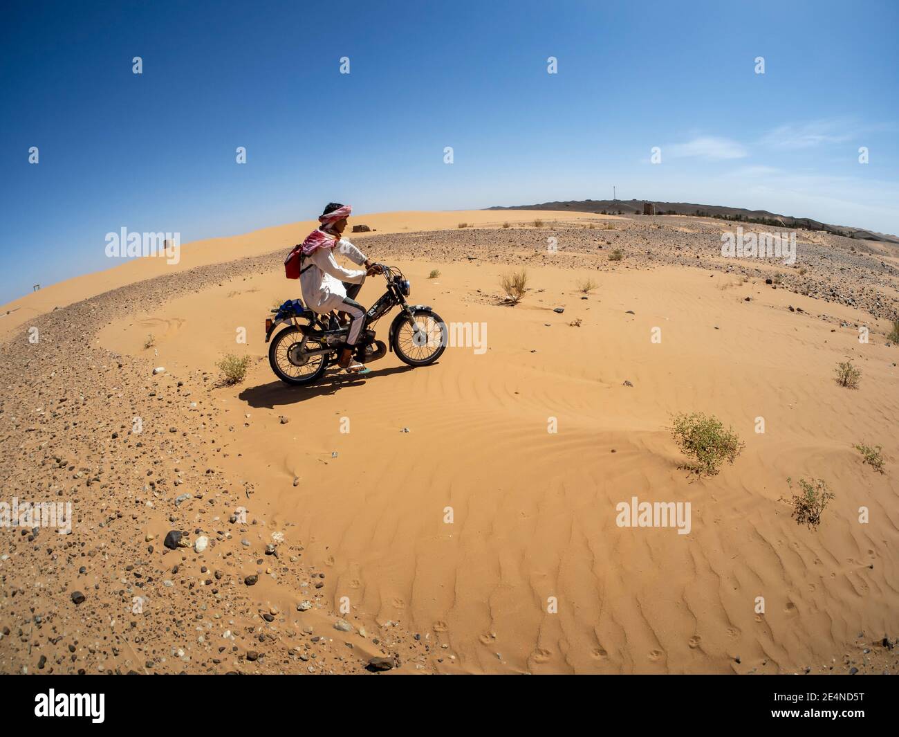 A Moroccan boy, wearing a turban, rides a motorcycle in summer through ...