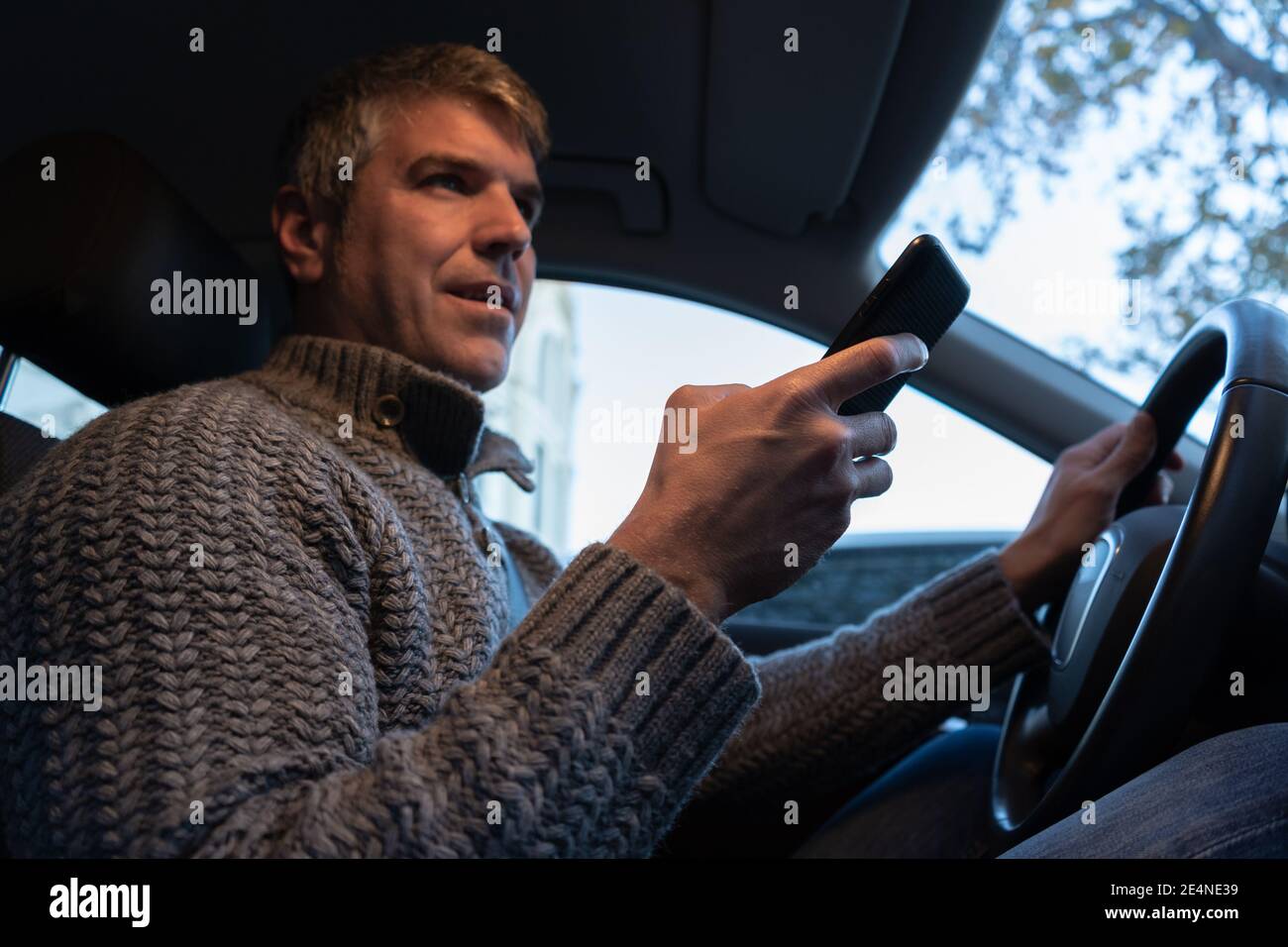Portrait of a young man who uses a smartphone while driving a car. road ...