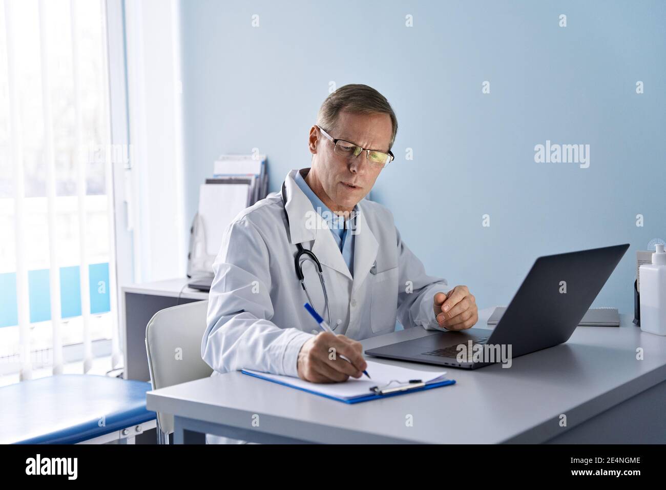 Old doctor using laptop in hospital watching medical webinar, writing ...
