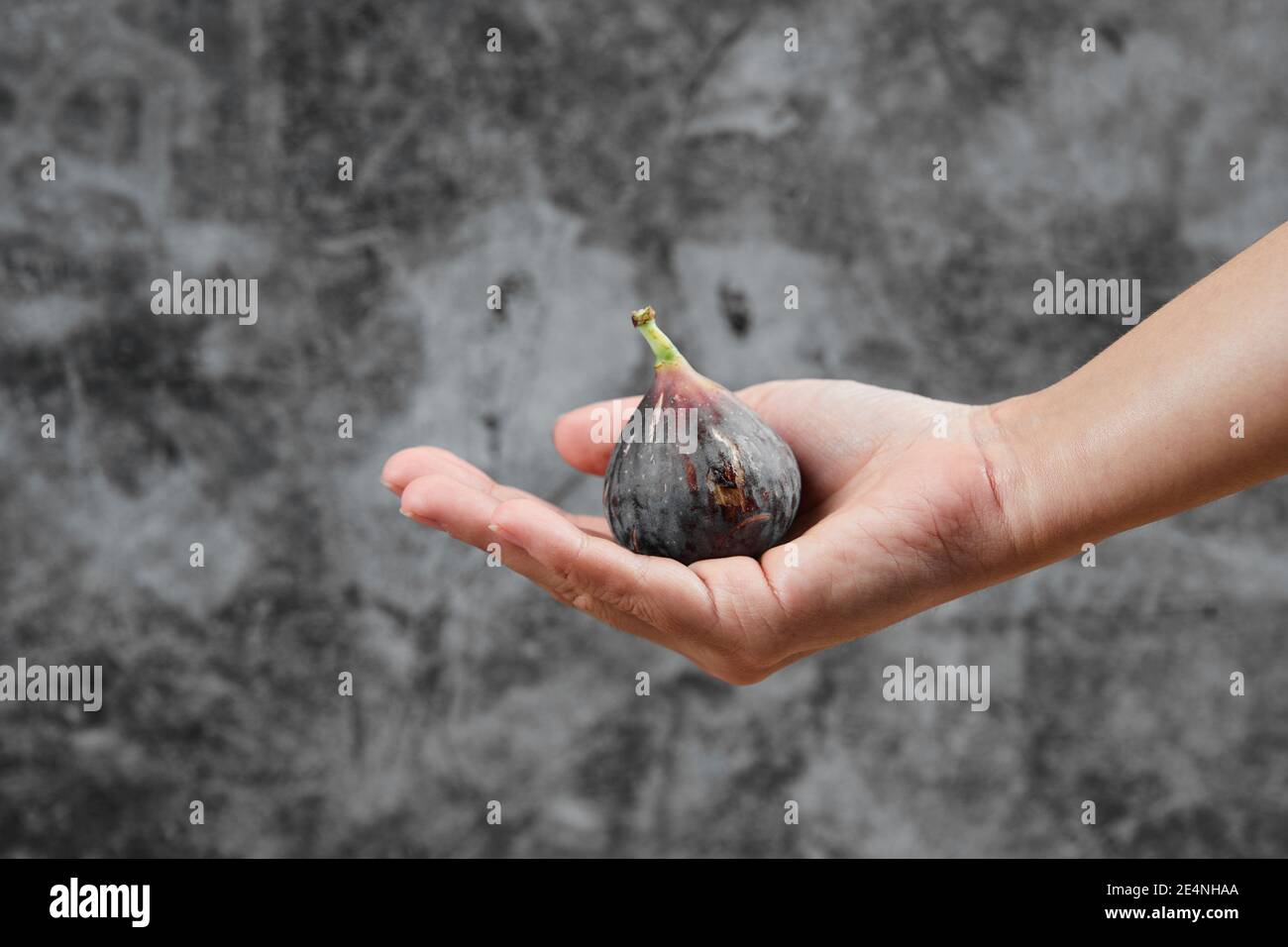 Hand holding a purple fig on a marble background Stock Photo - Alamy