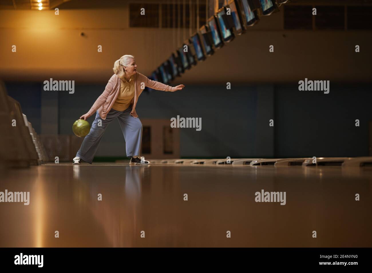 Wide angle side view at senior woman playing bowling alone while ...