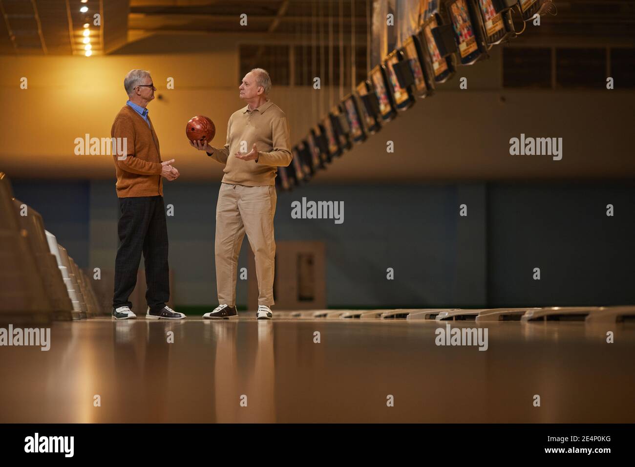Wide angle side view at two senior friends playing bowling together ...