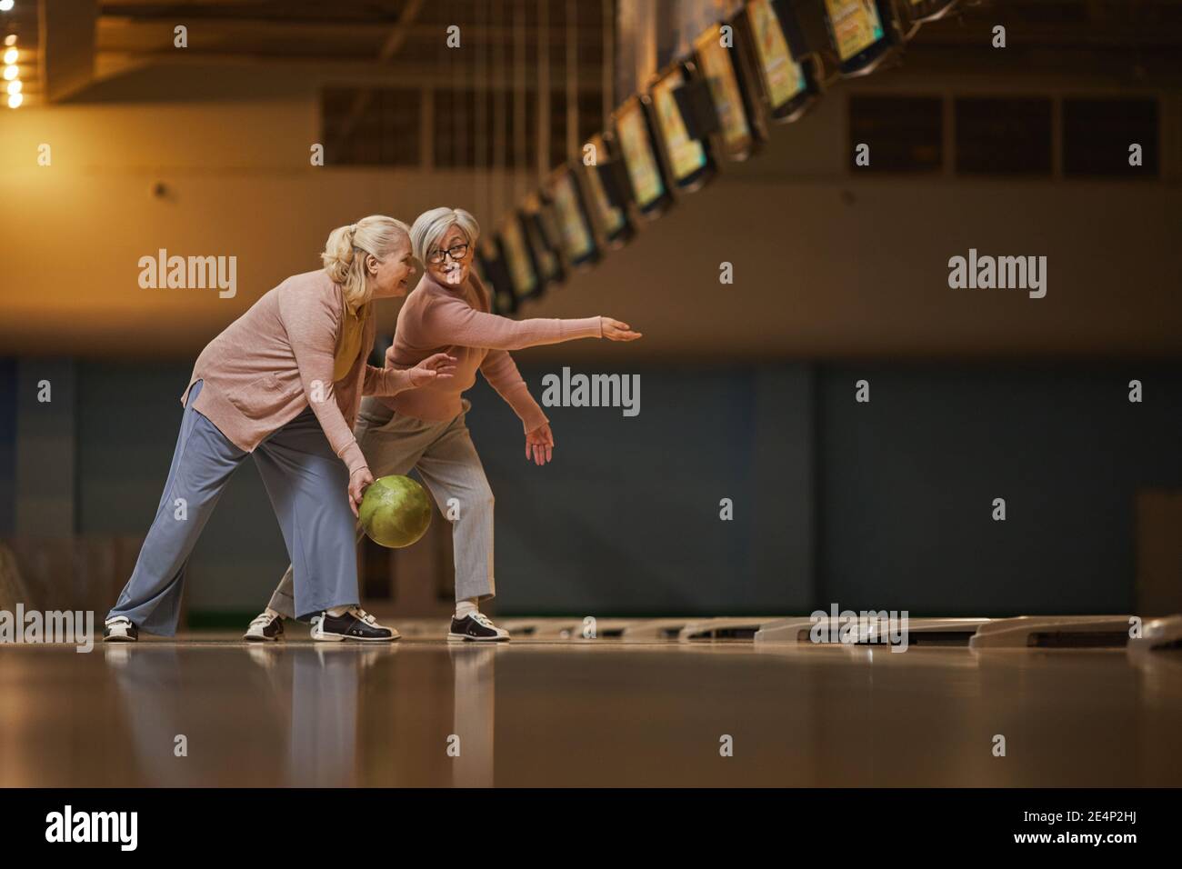 Wide angle side view at two senior women playing bowling together while ...