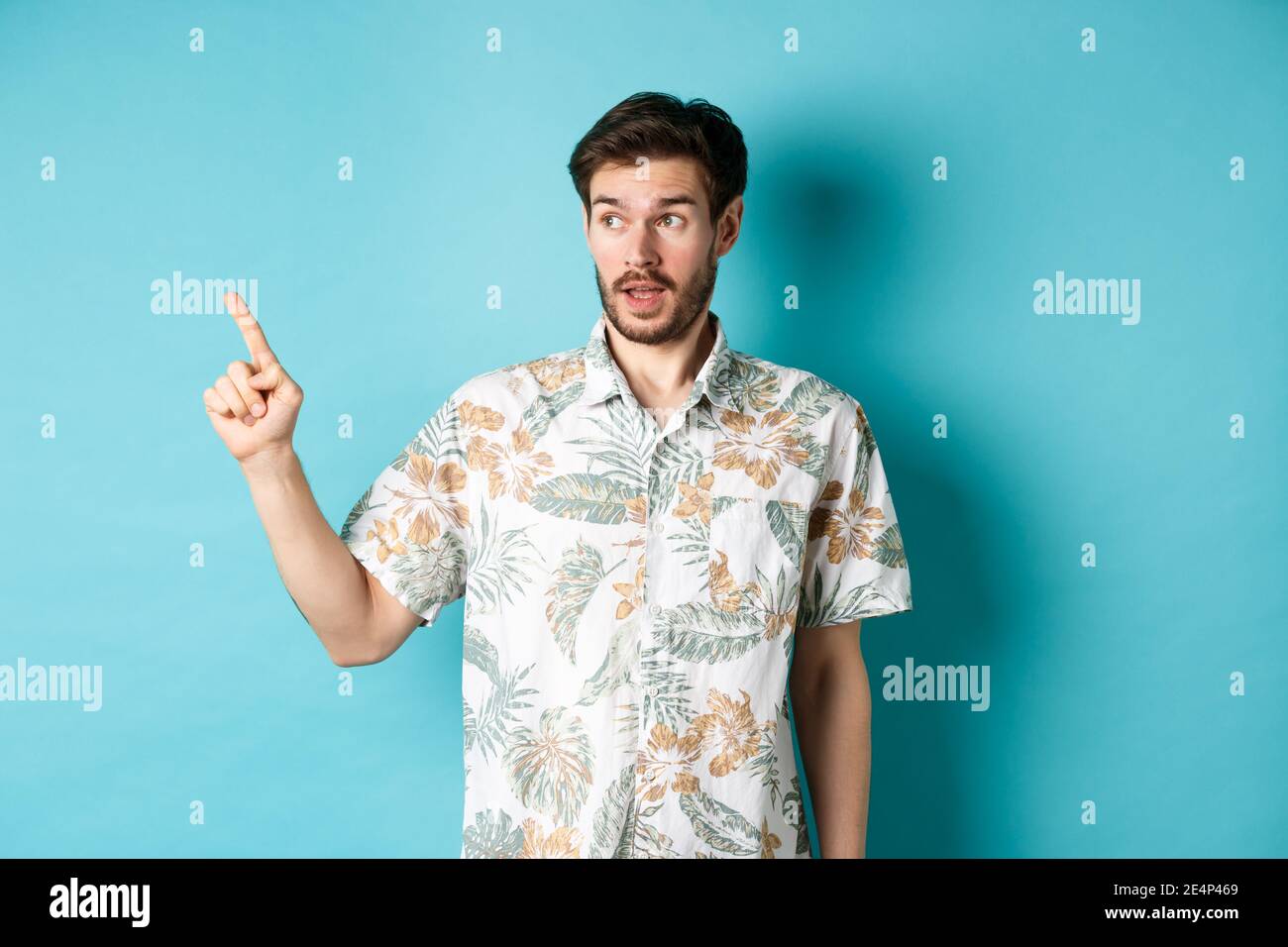 Intrigued man in hawaiian shirt, looking and pointing left at something ...