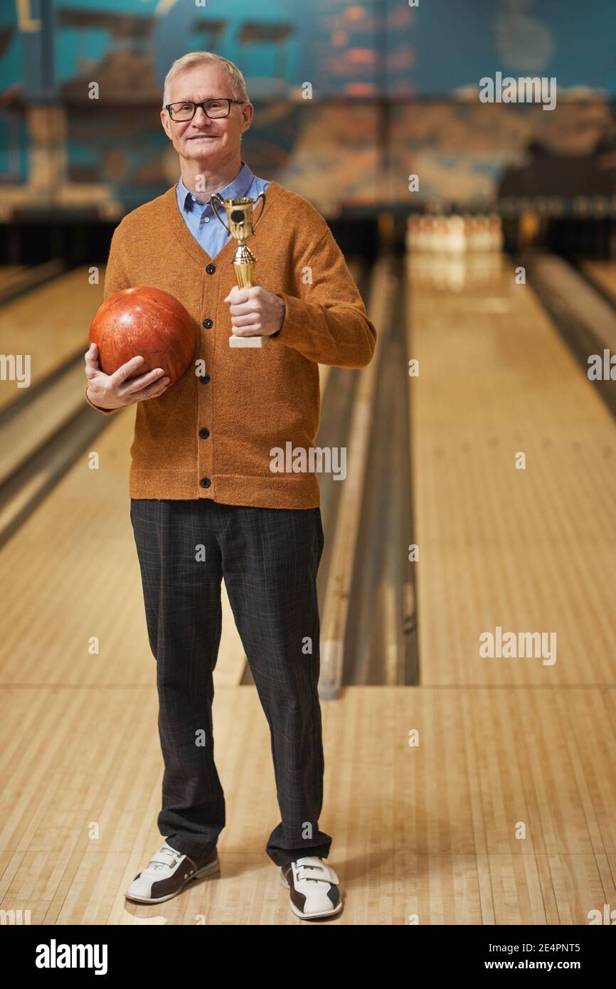 Vertical full length portrait of smiling senior man holding trophy and ...