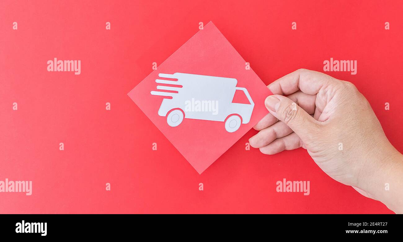 A female hand holding delivery truck shape symbol on red background ...